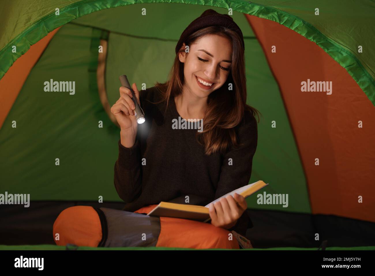 Young woman with flashlight reading book in tent Stock Photo - Alamy