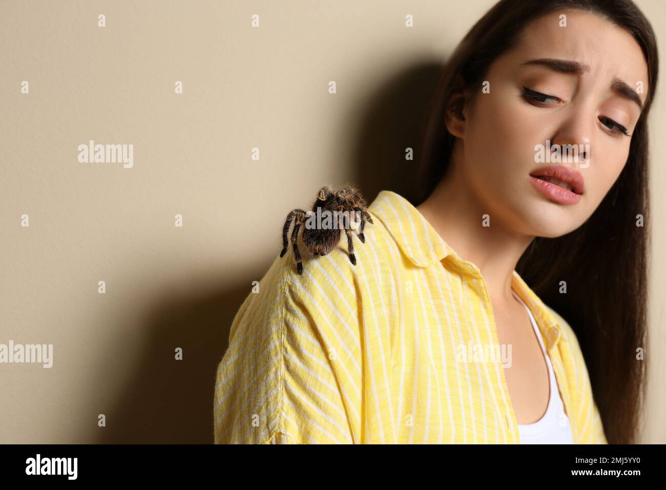 Scared young woman with tarantula on beige background. Arachnophobia ...