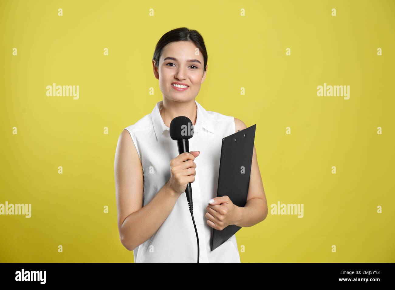Young female journalist with microphone and clipboard on yellow ...