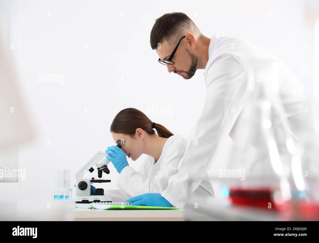 Scientist using microscope at table and colleague in laboratory ...