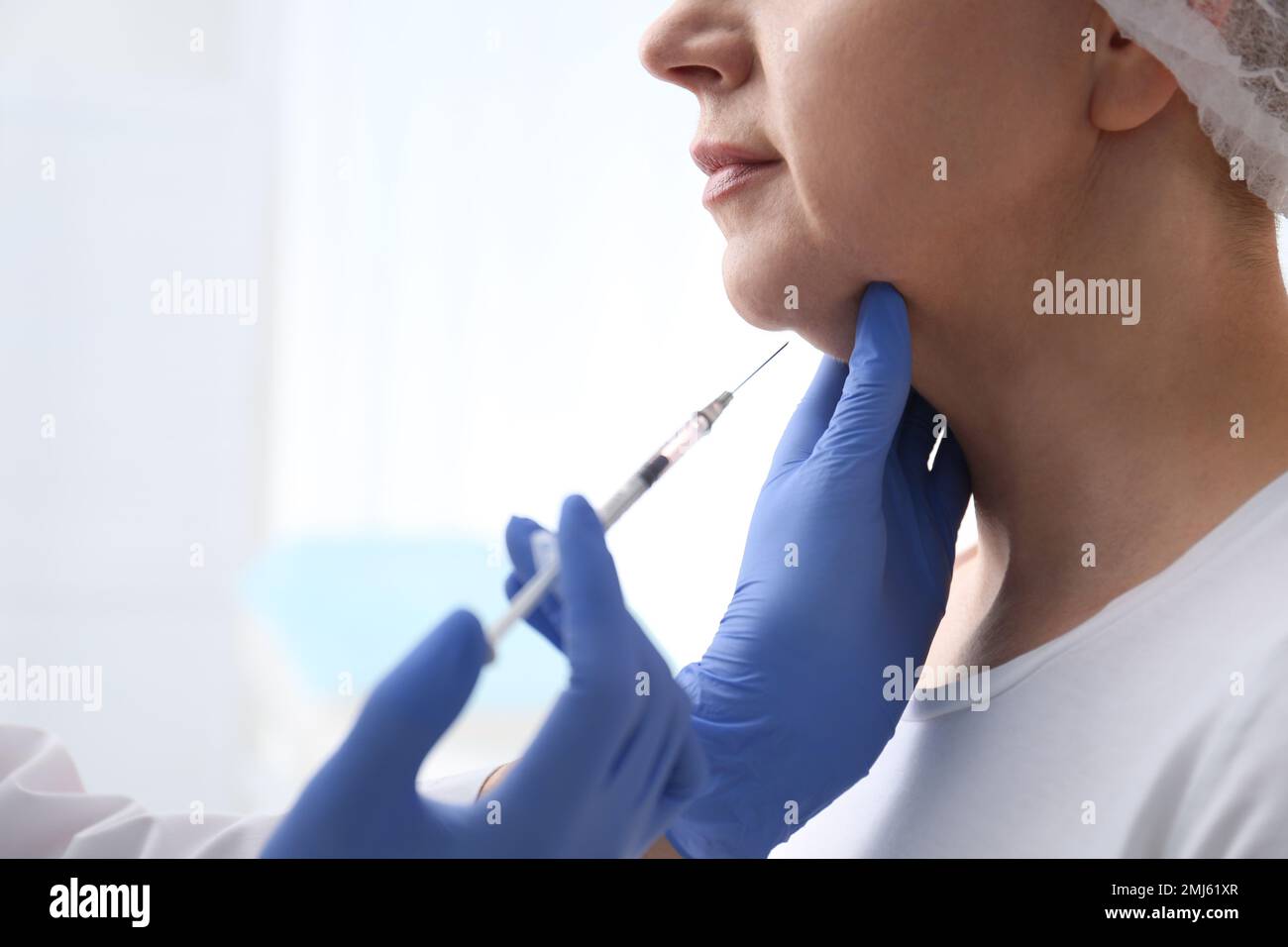 Mature woman with double chin receiving injection in clinic, closeup ...