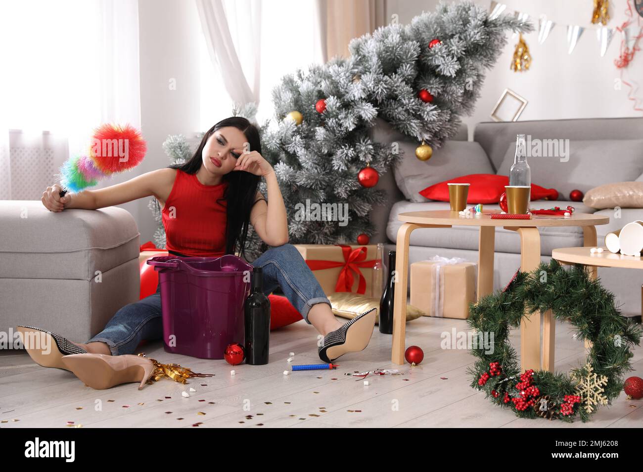 Young woman with dusting brush suffering from hangover in messy room ...