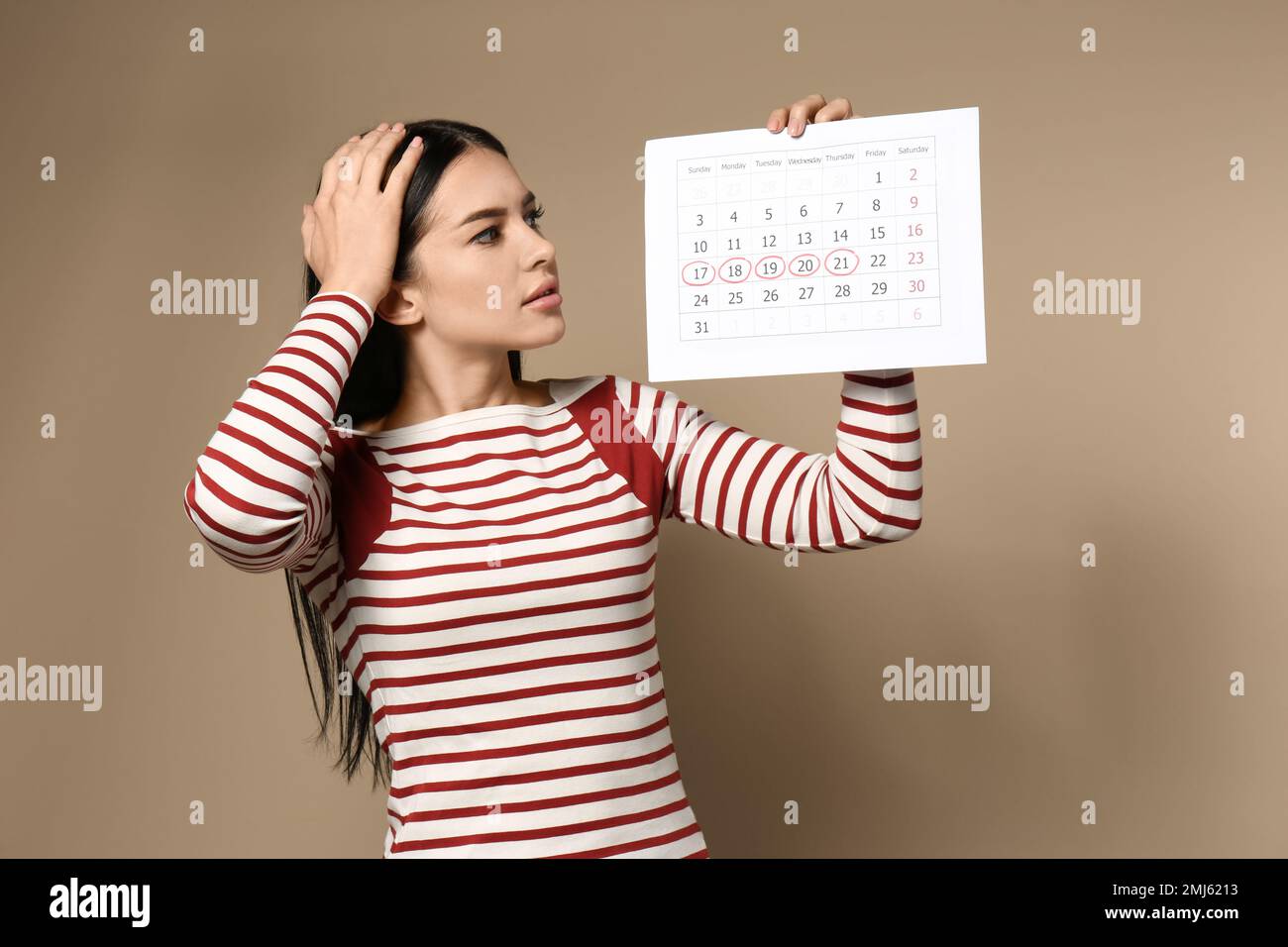 Emotional young woman holding calendar with marked menstrual cycle days ...