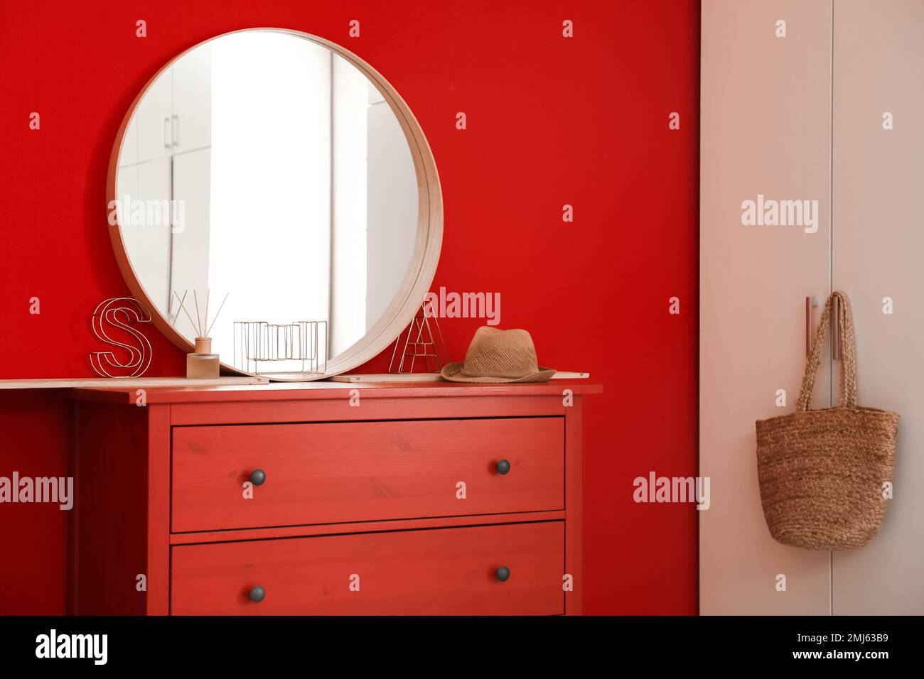 Round mirror and chest of drawers near red wall in room. Modern ...