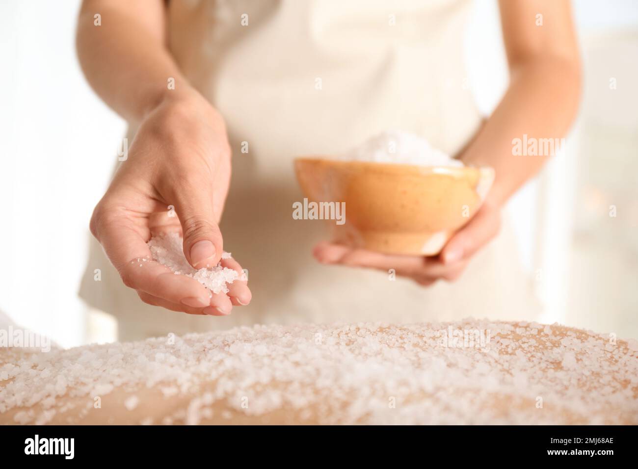 Young woman having body scrubbing procedure with sea salt in spa salon ...