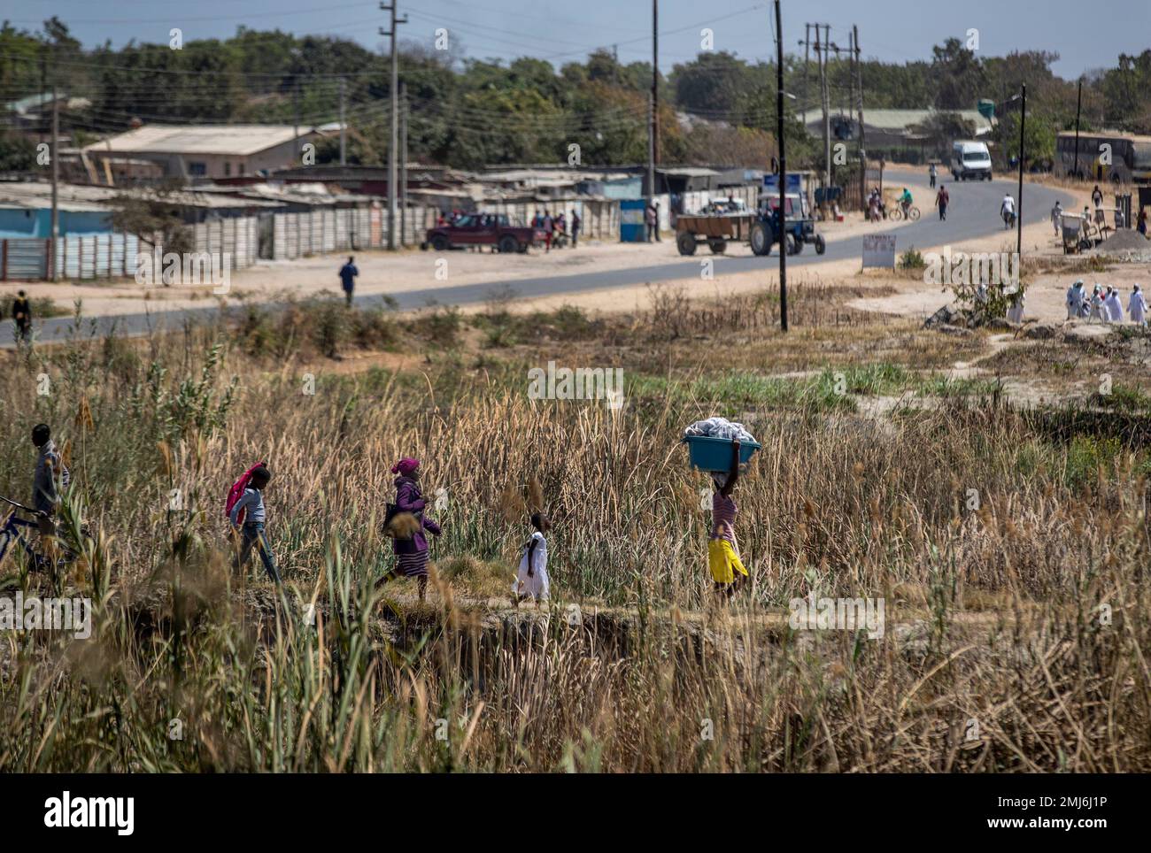Zimbabwean women and girls walk down a path as they return from church ...