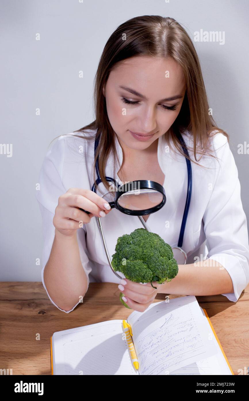 A female nutritionist looks through a magnifying glass at broccoli in ...