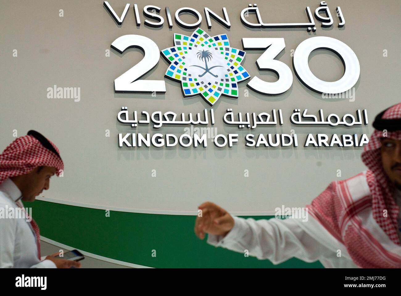 Saudi men walk past a "Vision 2030" display at a stand about Saudi ...