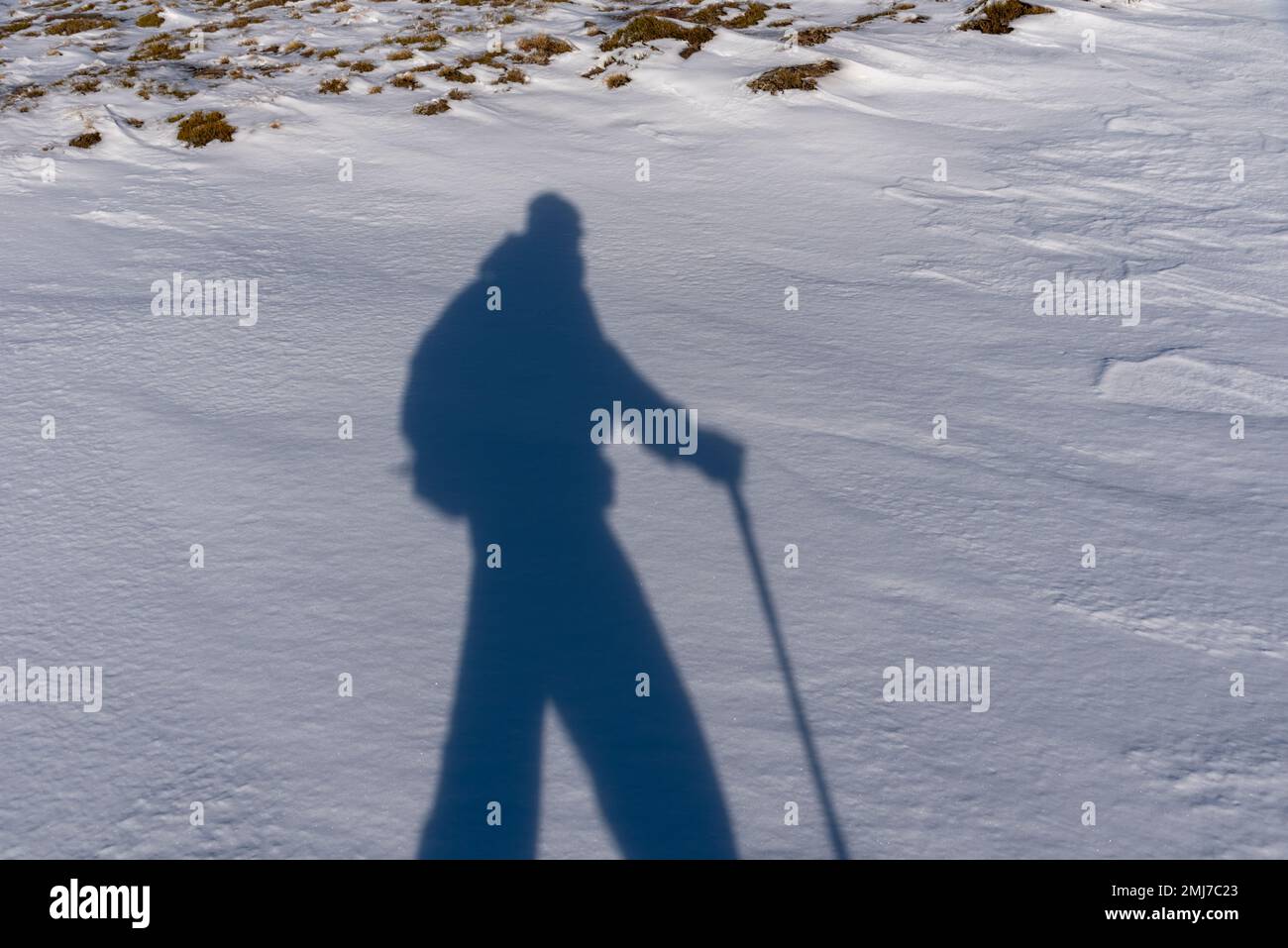 Shadow of a mountaineer reflected in the snow walking with a backpack ...
