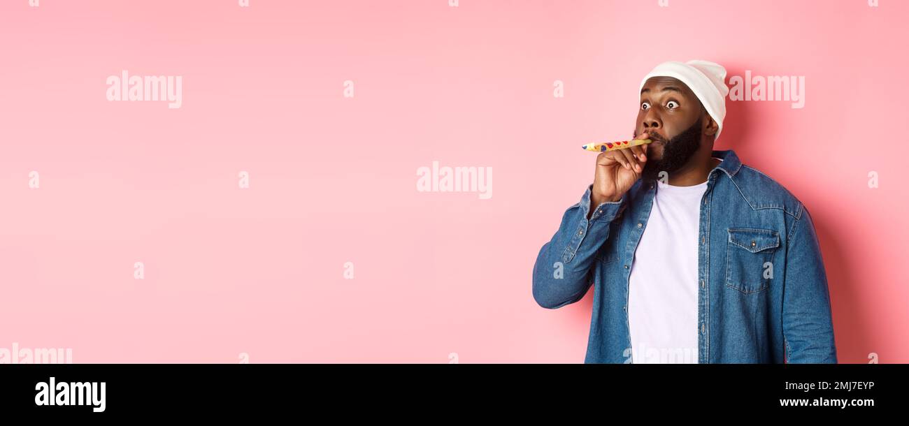 Funny Black man blowing in party whistle and pouting, staring sideways ...