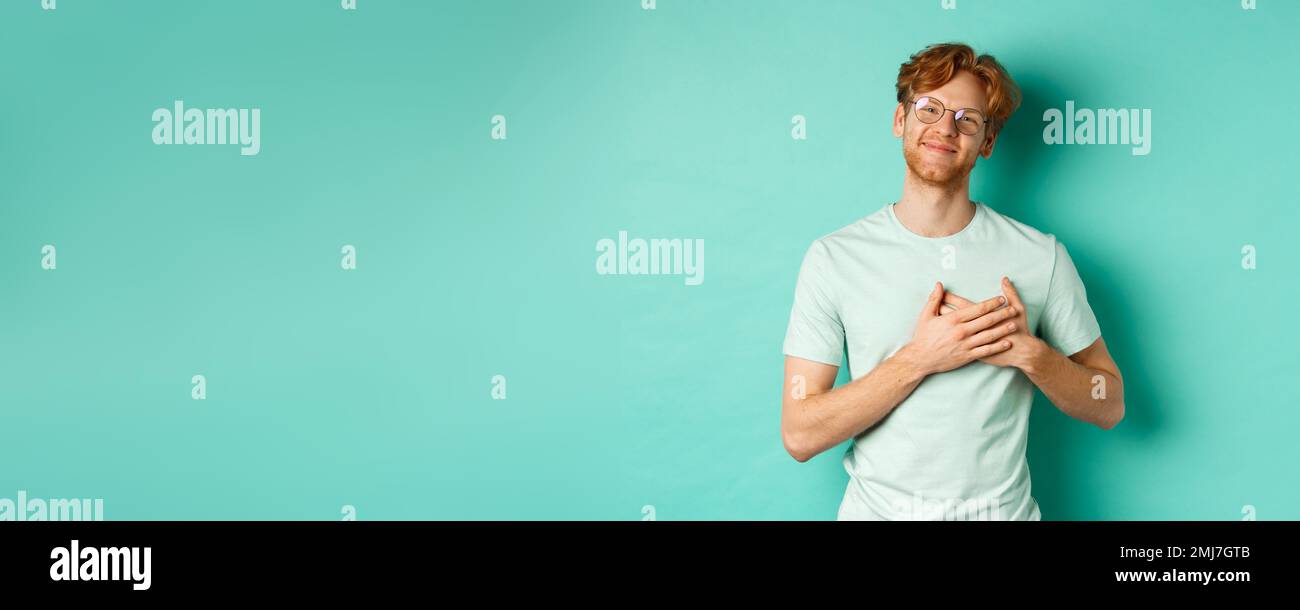 Handsome young man with red hair and glasses, holding hands on heart ...