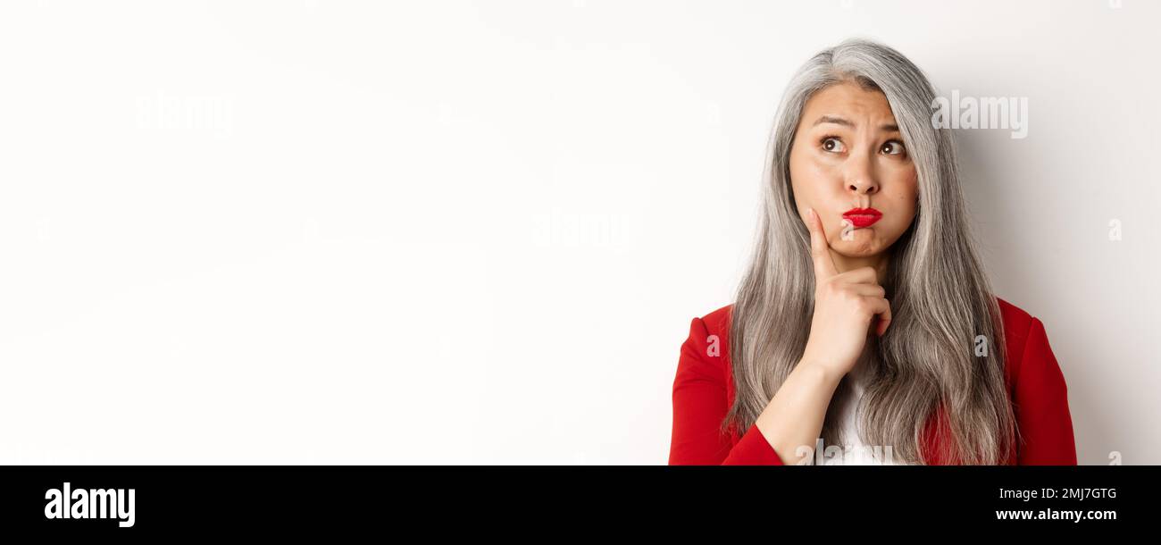 Close up of indecisive asian senior woman making choice, pouting and ...