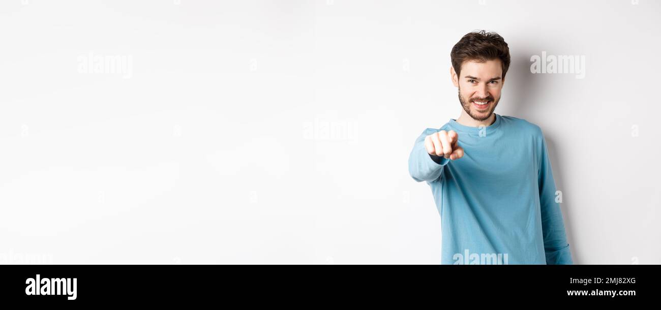 Image of confident young man smiling and pointing at camera, inviting ...