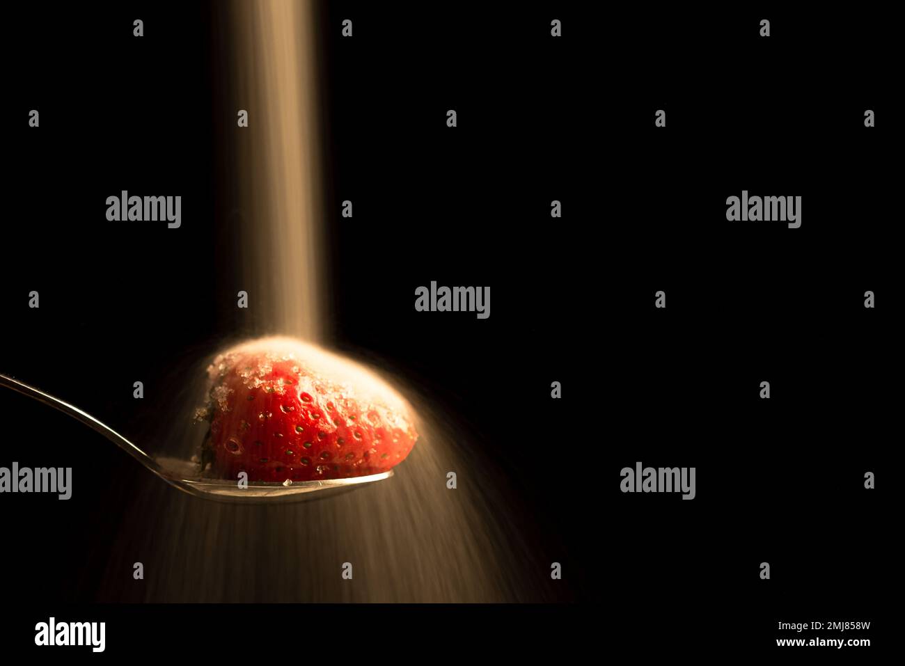Sugar being poured on a strawberry with a dark background, copy space ...