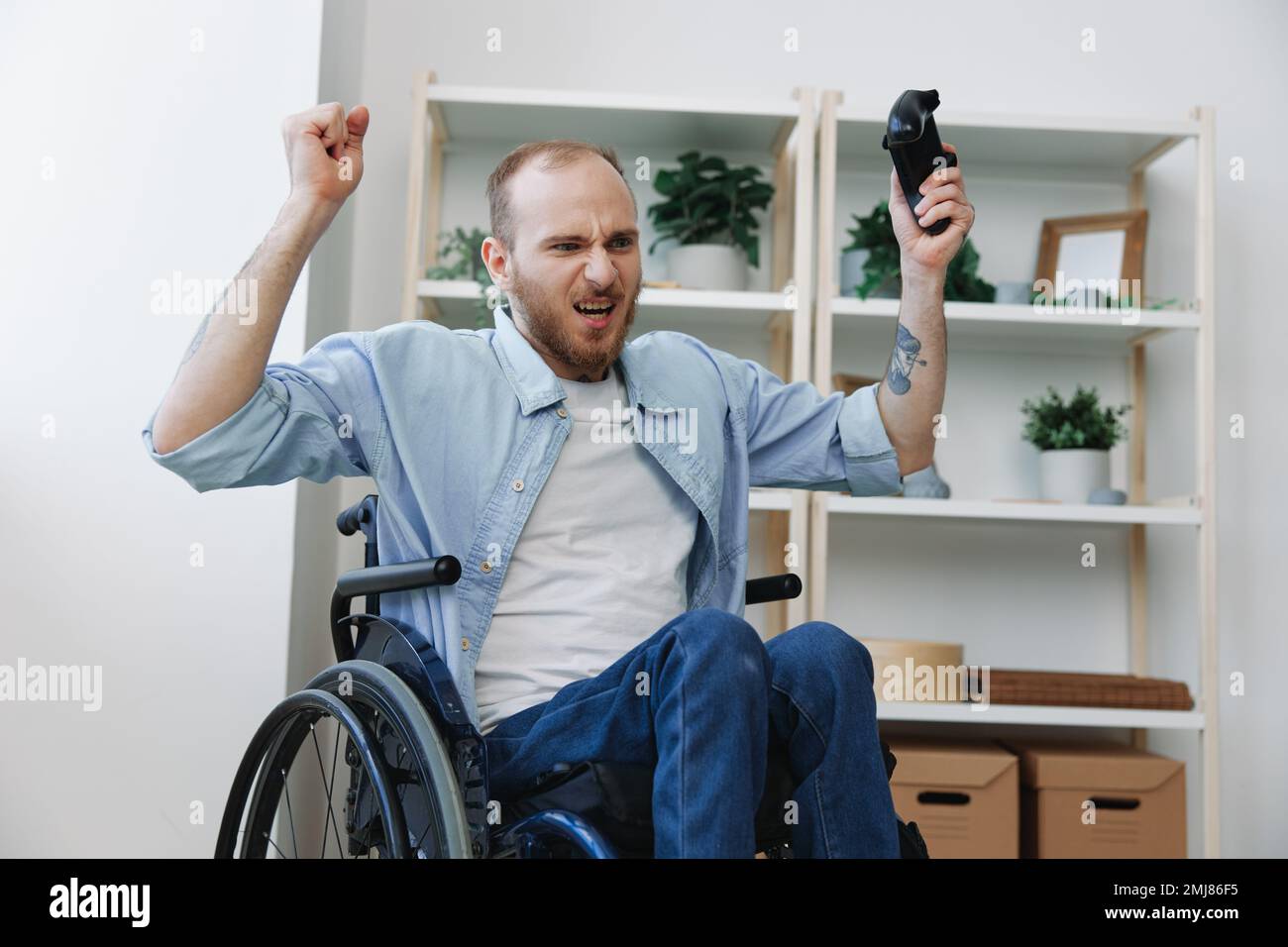 A man in a wheelchair gamer plays games with a joystick in his hands at ...