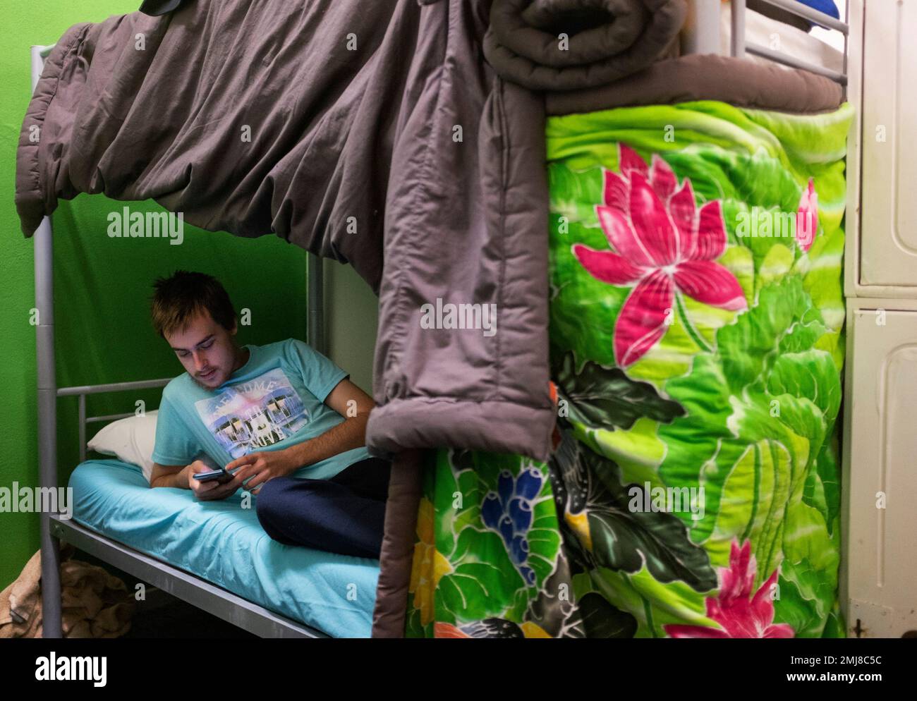 Sam Ware, 22, plays on his phone before going to bed at a hostel in The ...