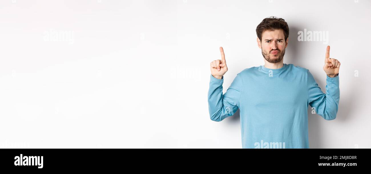 Disappointed male model frowning and sulking, pointing fingers up with ...