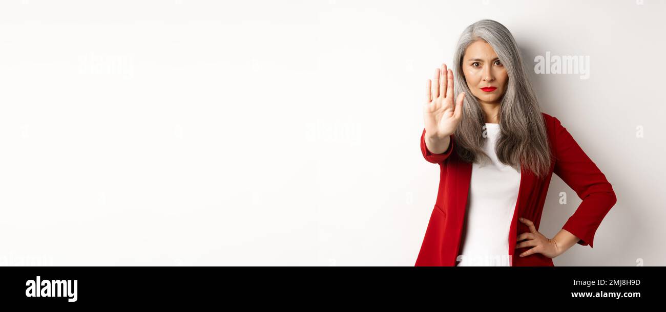 Serious asian woman in red blazer showing stop sign, telling no ...