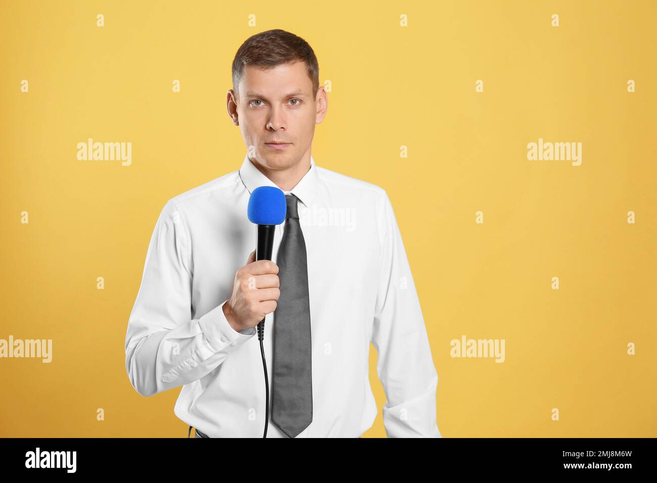Male journalist with microphone on yellow background Stock Photo - Alamy
