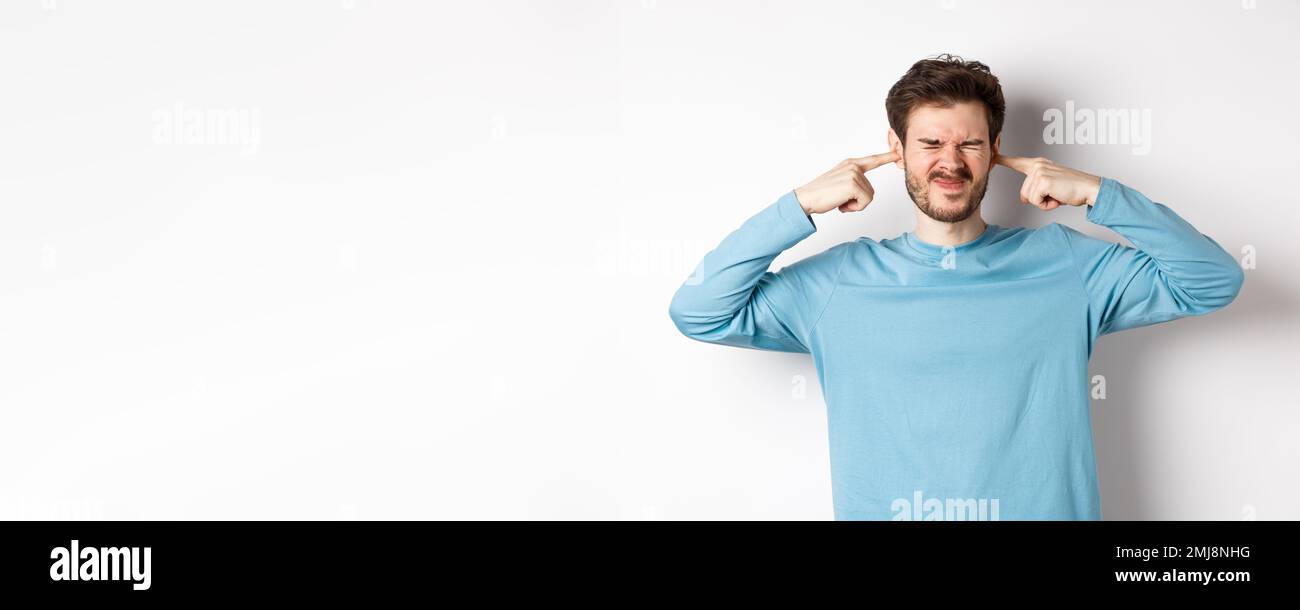 Annoyed young man plug ears from loud awful sound, being disturbed by ...