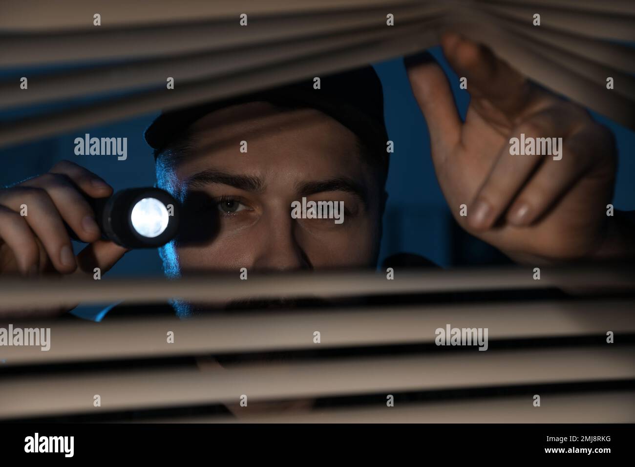 Male security guard with flashlight looking through window blinds in ...