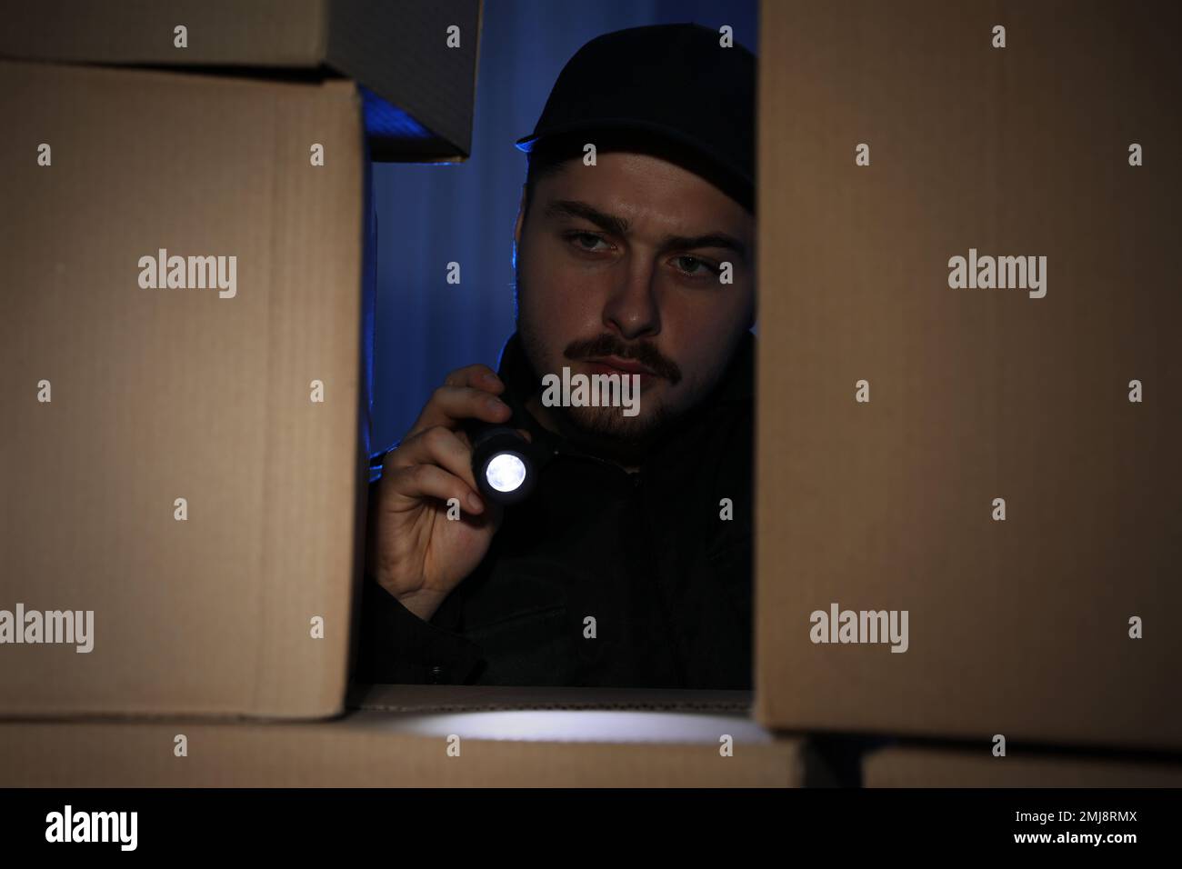Security guard with flashlight looking through pile of cardboard boxes ...