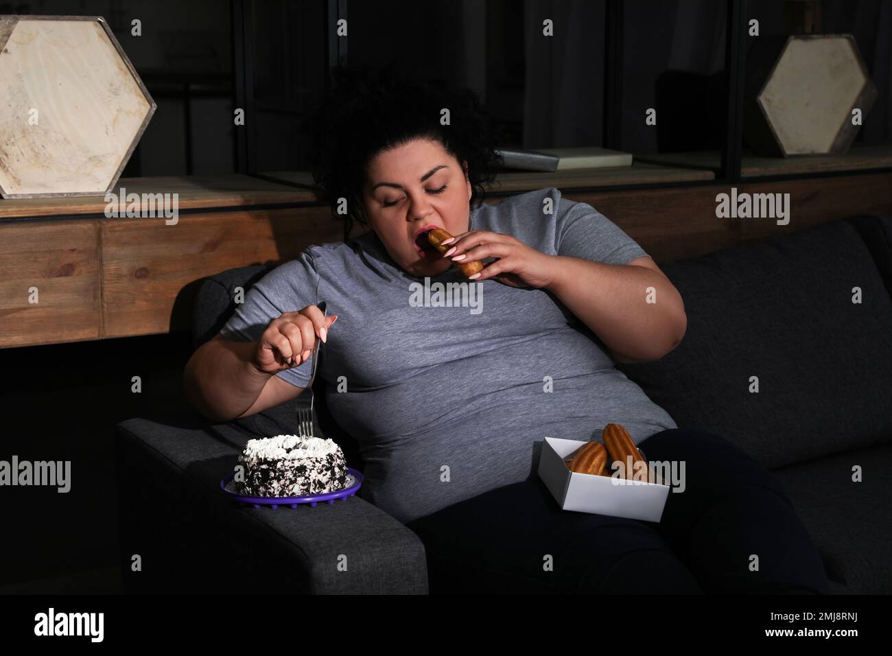 Depressed overweight woman eating sweets in living room at night Stock ...