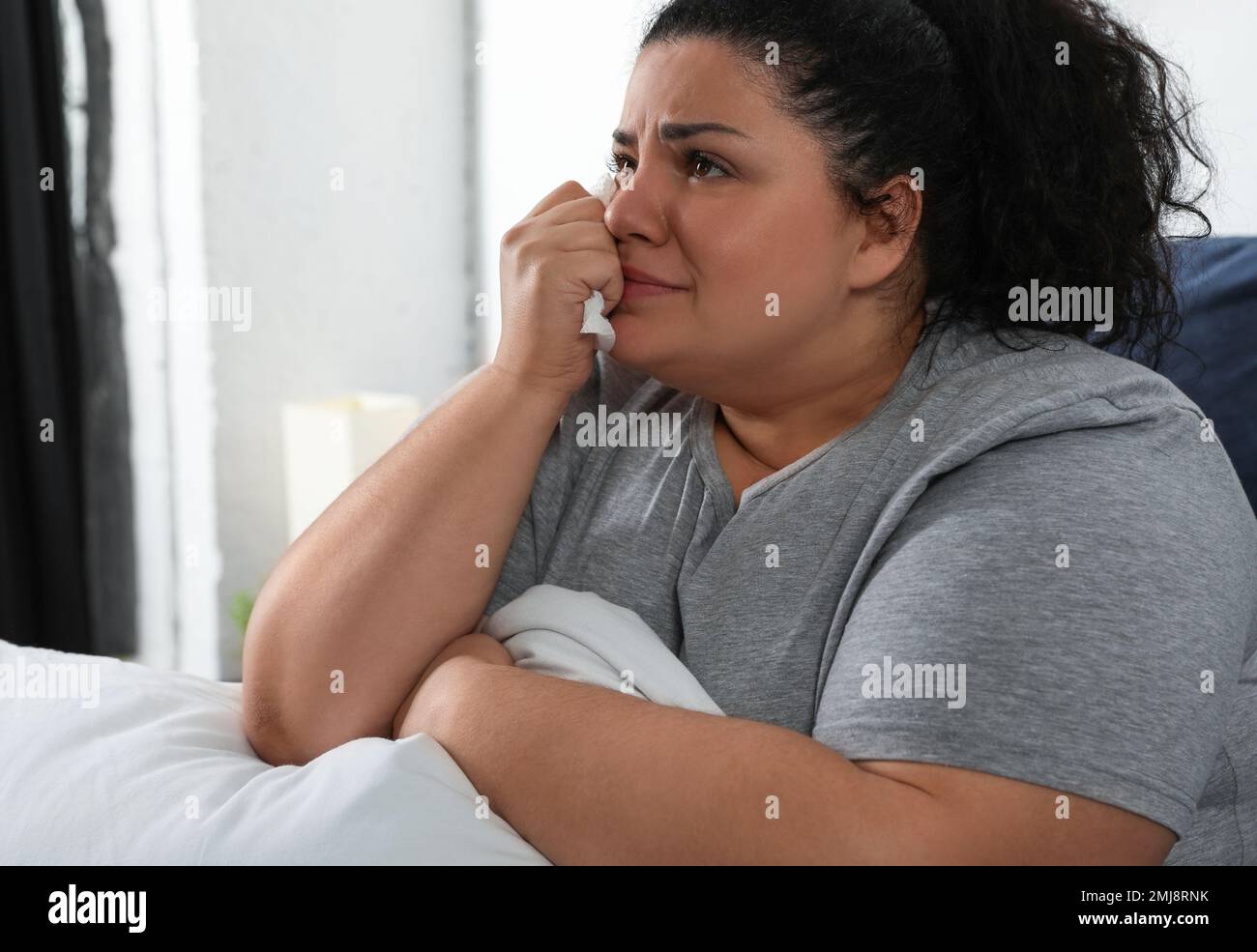 Depressed overweight woman crying while hugging pillow on bed Stock ...