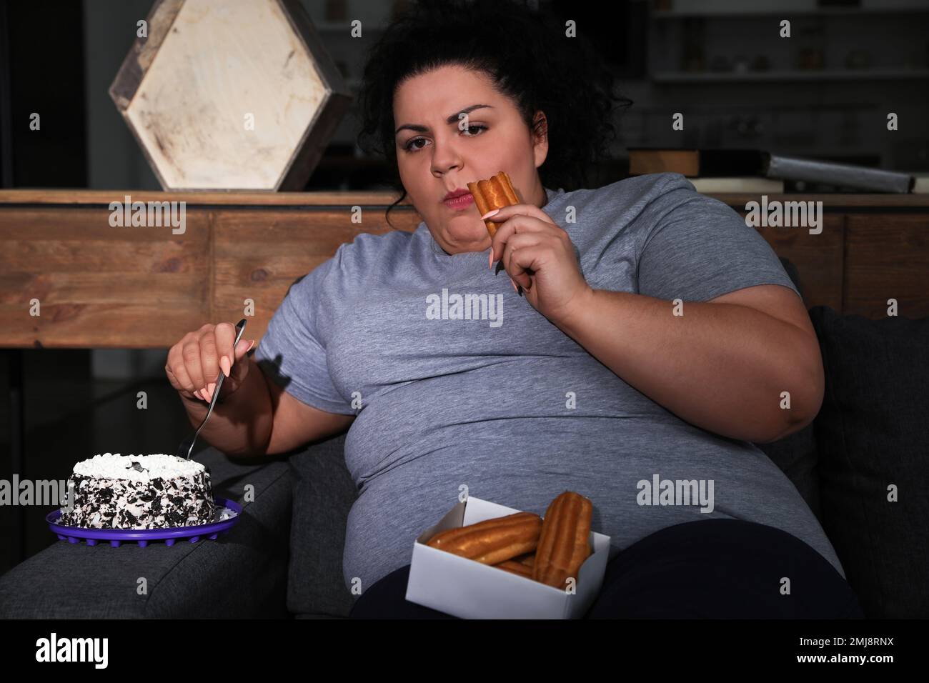 Depressed overweight woman eating sweets in living room at night Stock ...