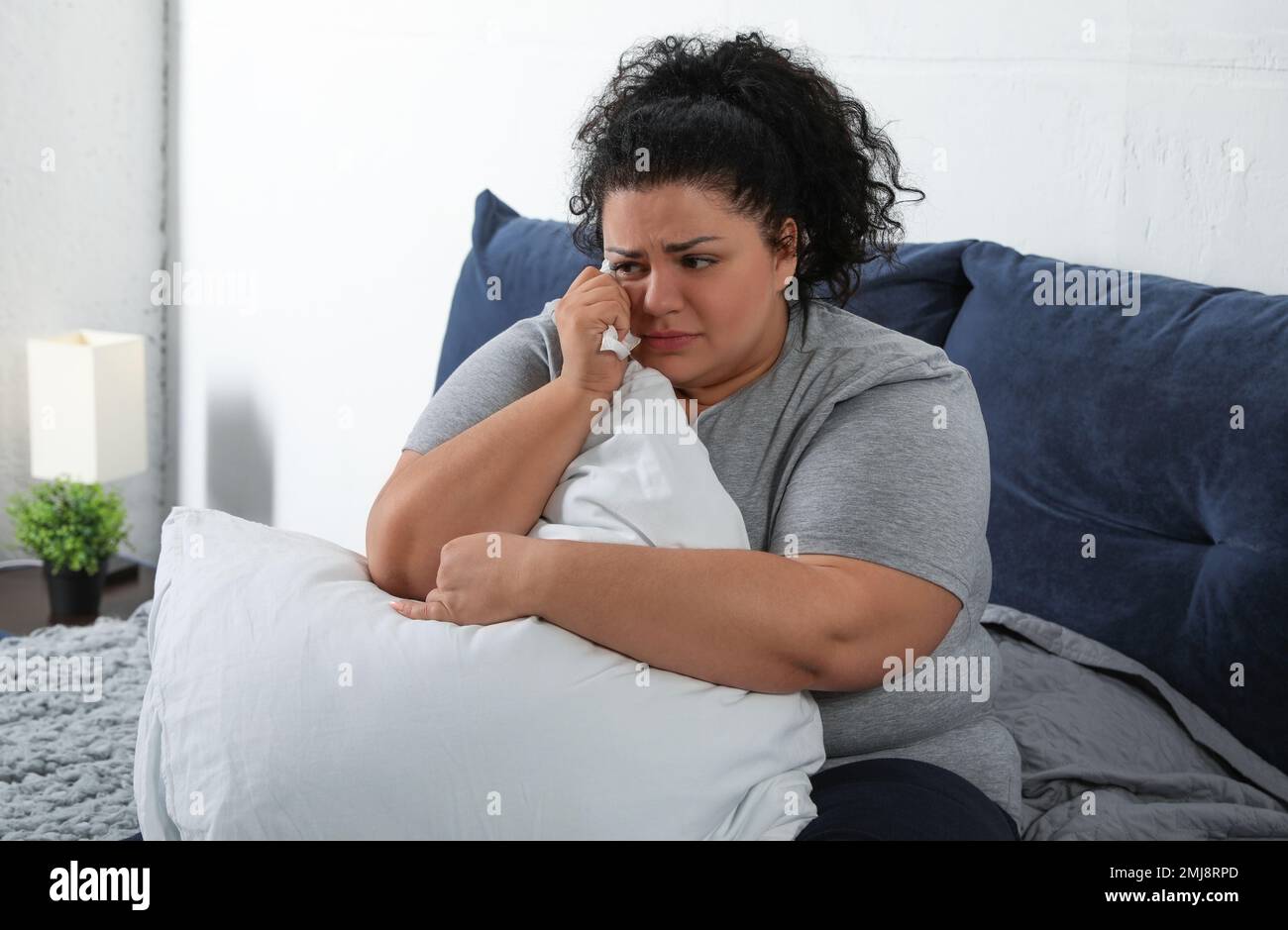 Depressed overweight woman crying while hugging pillow on bed Stock ...