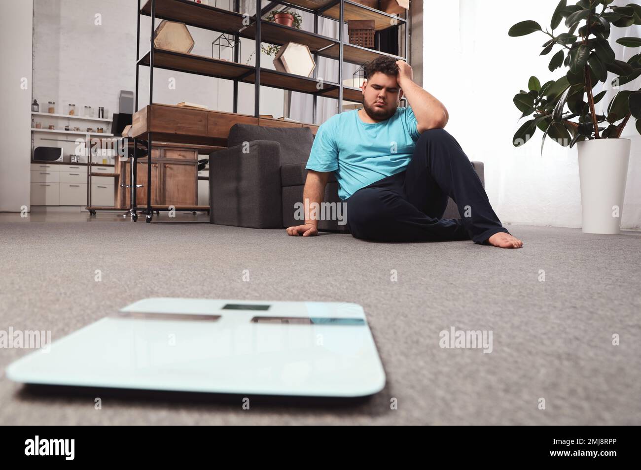 Scales and depressed overweight man on floor at home Stock Photo - Alamy