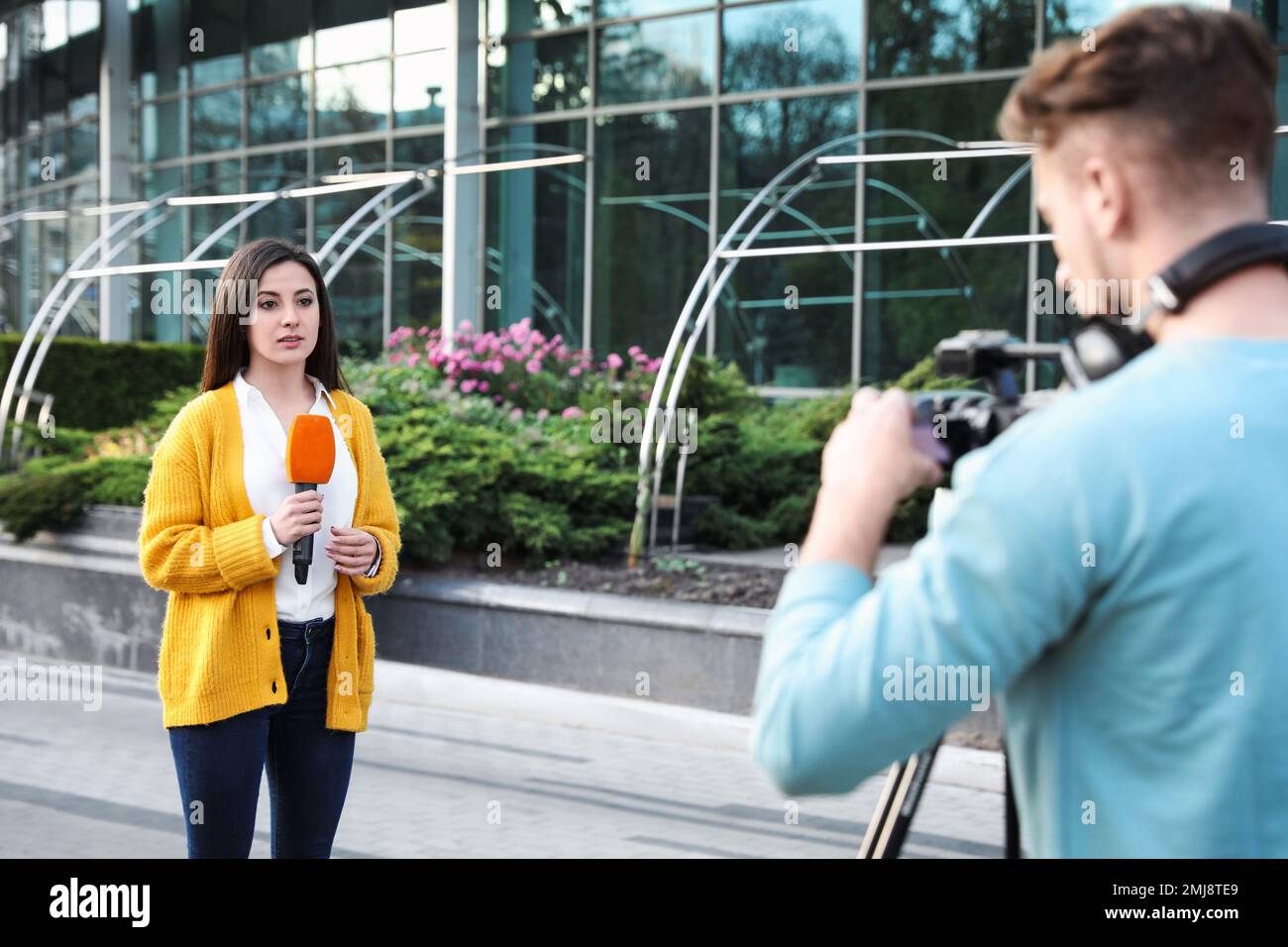 Young journalist and video operator working on city street Stock Photo ...