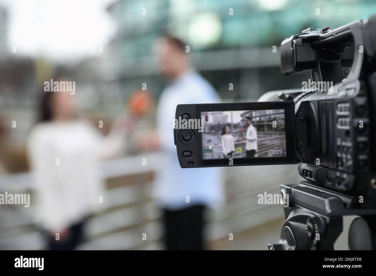 Young journalist interviewing man on city street, focus on camera ...