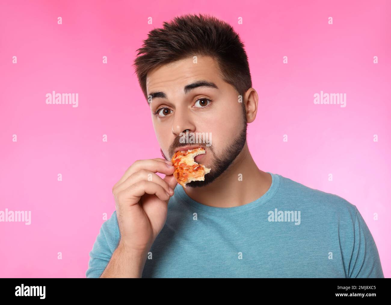 Emotional man eating pizza on pink background Stock Photo - Alamy