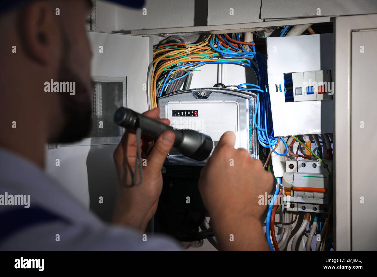 Electrician with flashlight fixing electric panel indoors Stock Photo ...