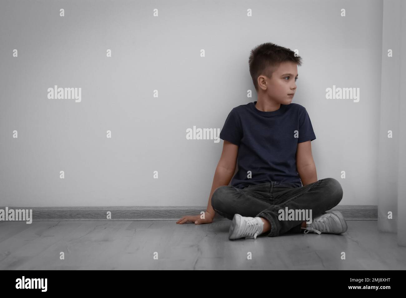 Sad little boy sitting on floor indoors, space for text. Child in ...