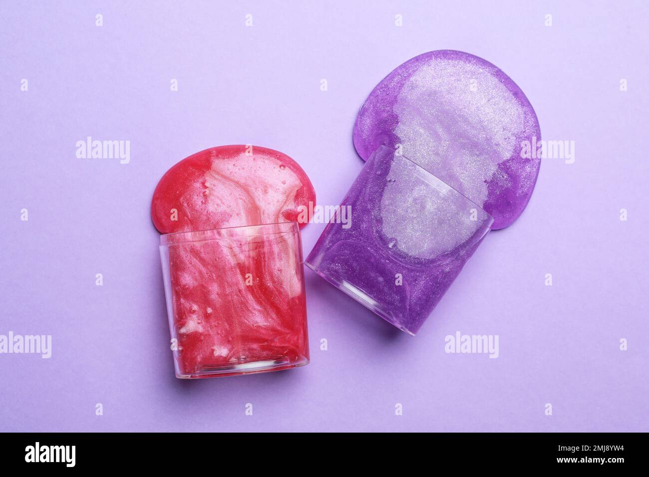 Overturned plastic containers with bright slimes on violet background ...