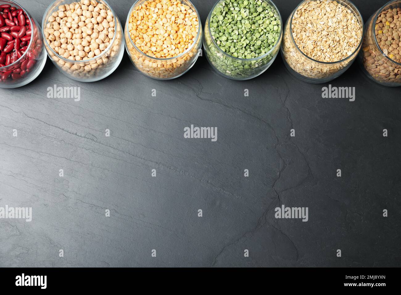 Glass jars with different types of groats on black table, flat lay ...