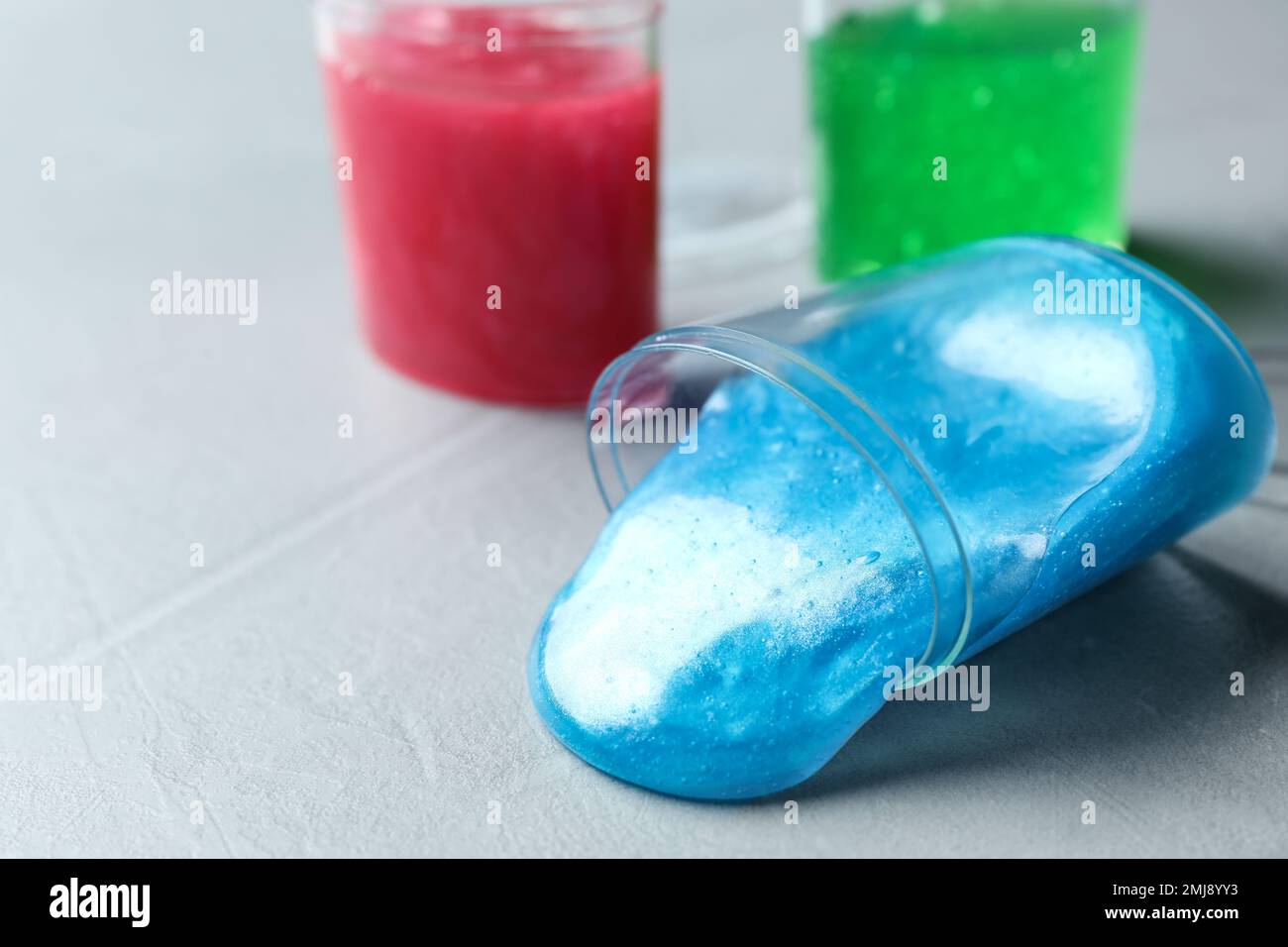Overturned plastic container with light blue slime on grey background ...