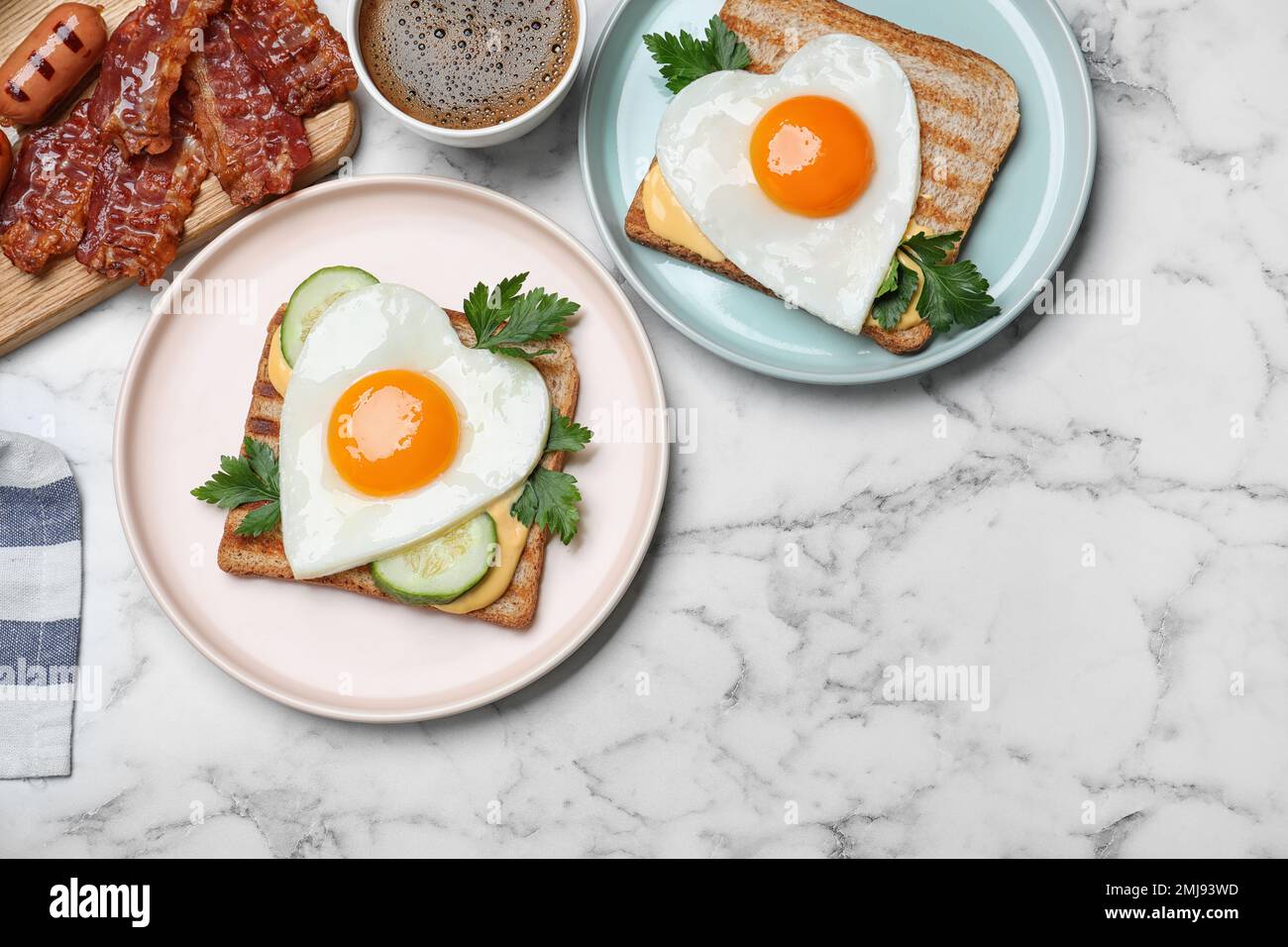 Tasty sandwiches with heart shaped fried eggs for romantic breakfast on white marble table, flat ...