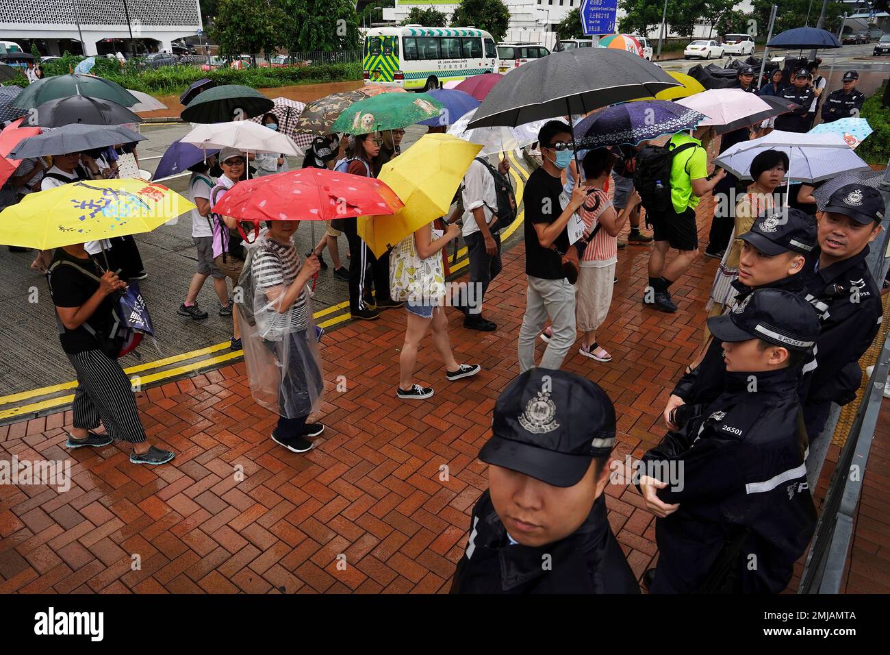 People carrying umbrellas march past police officers in the rain as ...