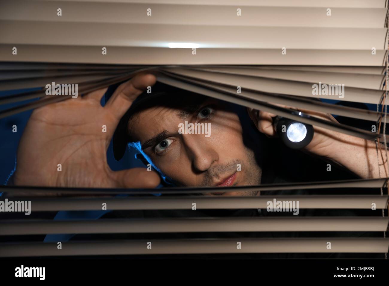 Male security guard with flashlight looking through window blinds in ...
