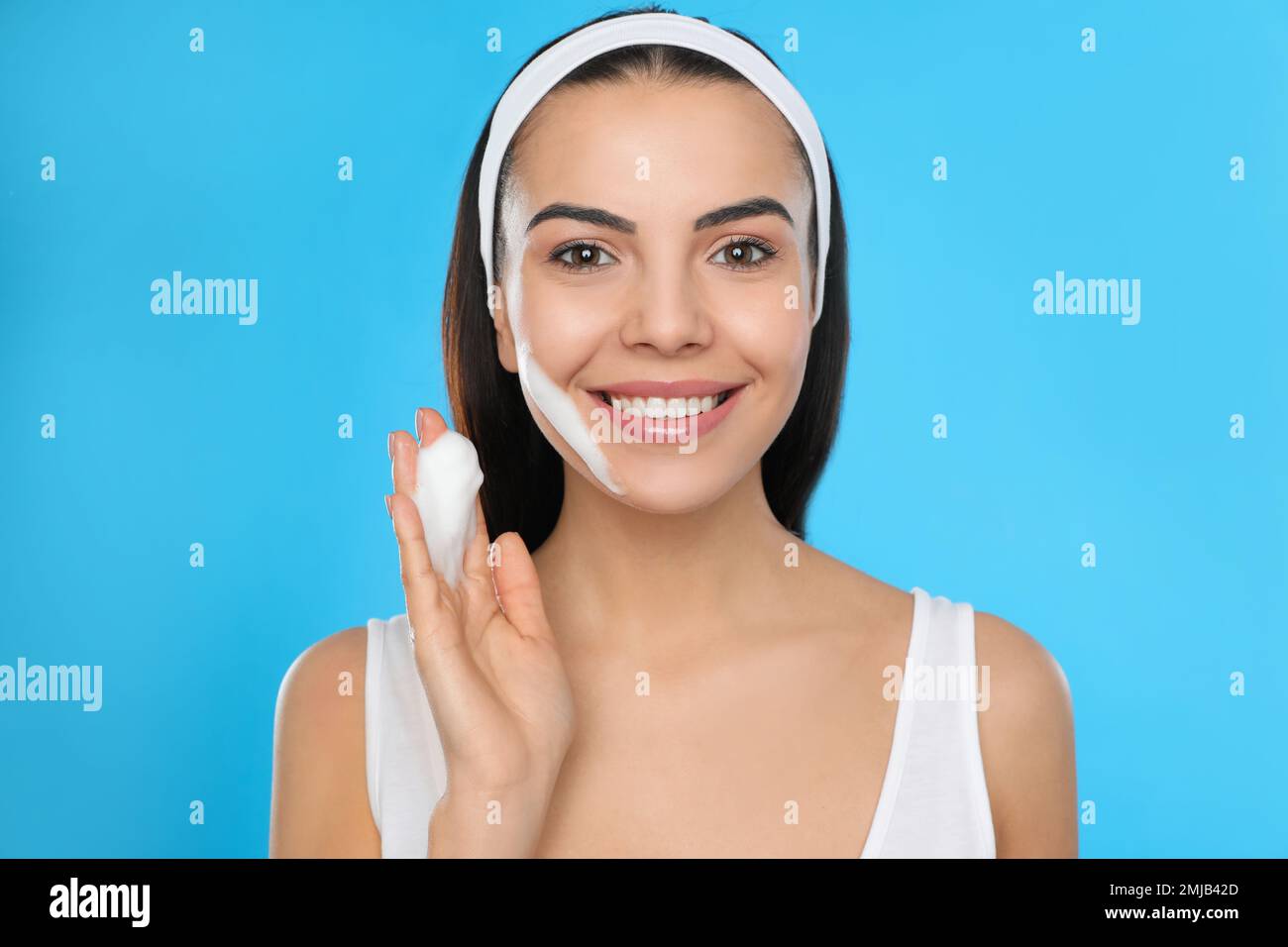 Young woman applying cosmetic product on light blue background. Washing ...