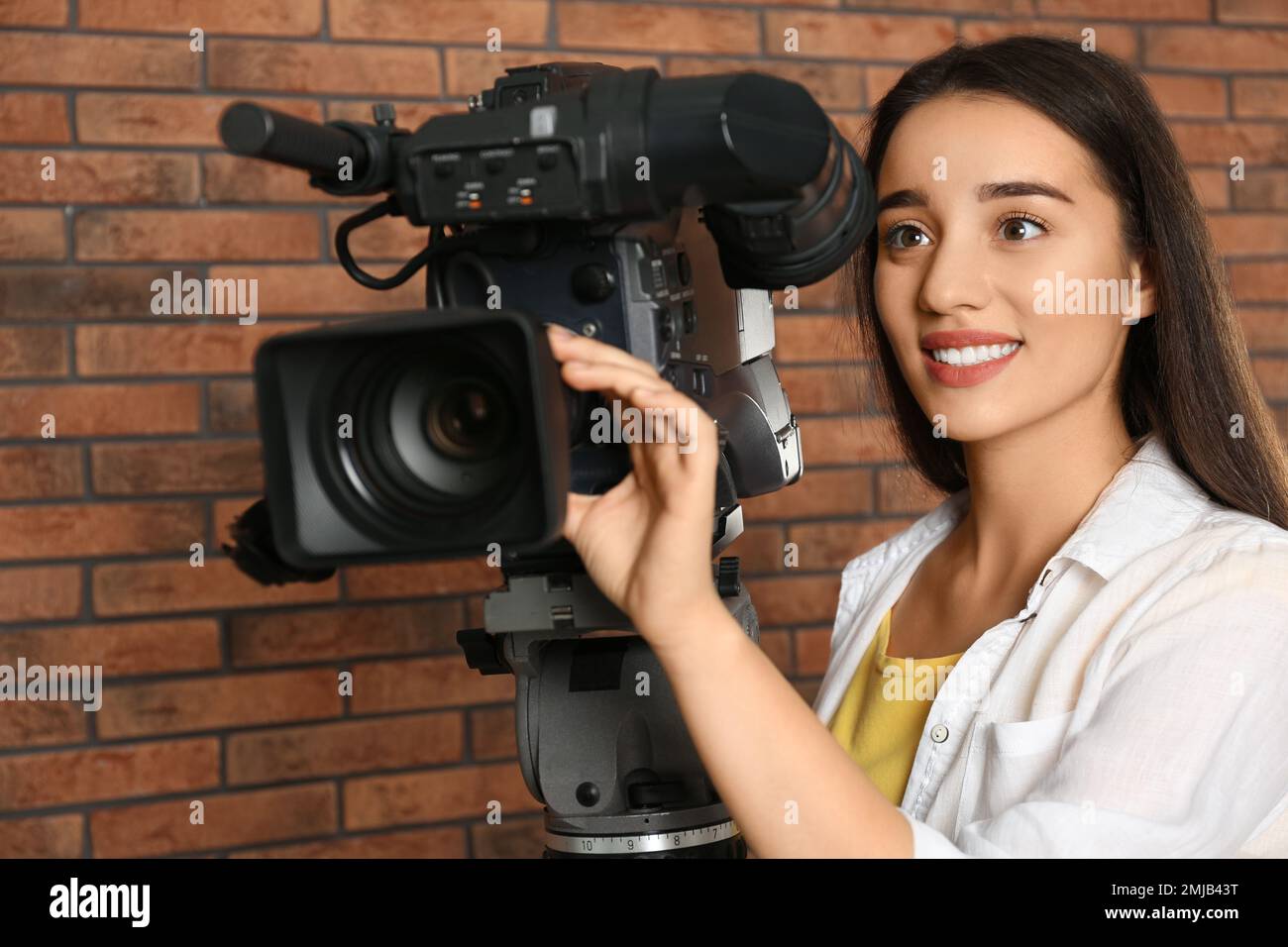 Operator with professional video camera near brick wall Stock Photo - Alamy