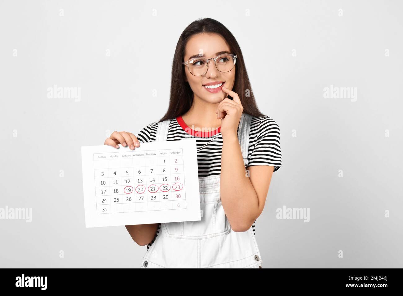 Young woman holding calendar with marked menstrual cycle days on light ...