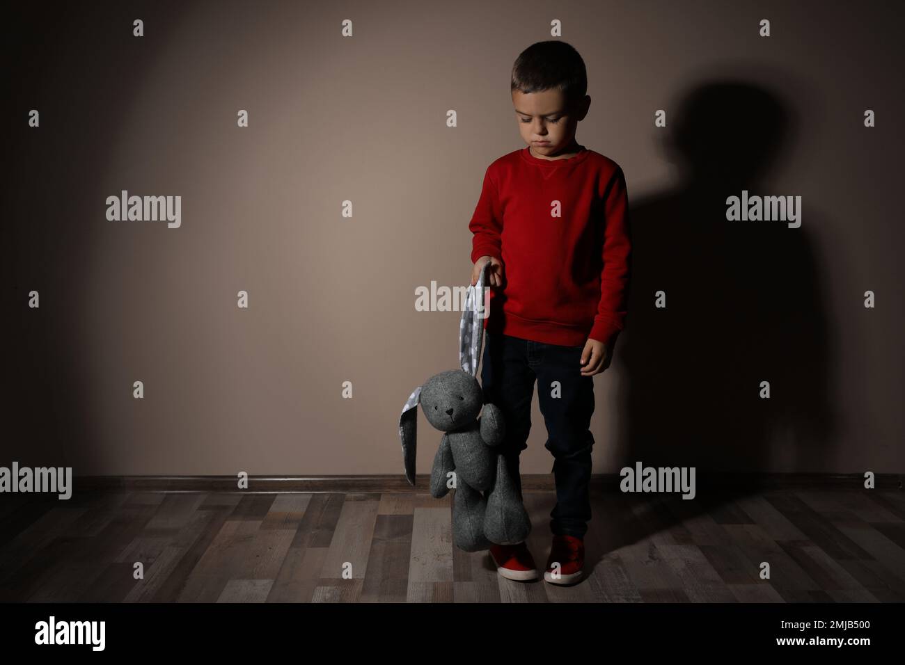 Sad little boy with toy near beige wall, space for text. Domestic ...