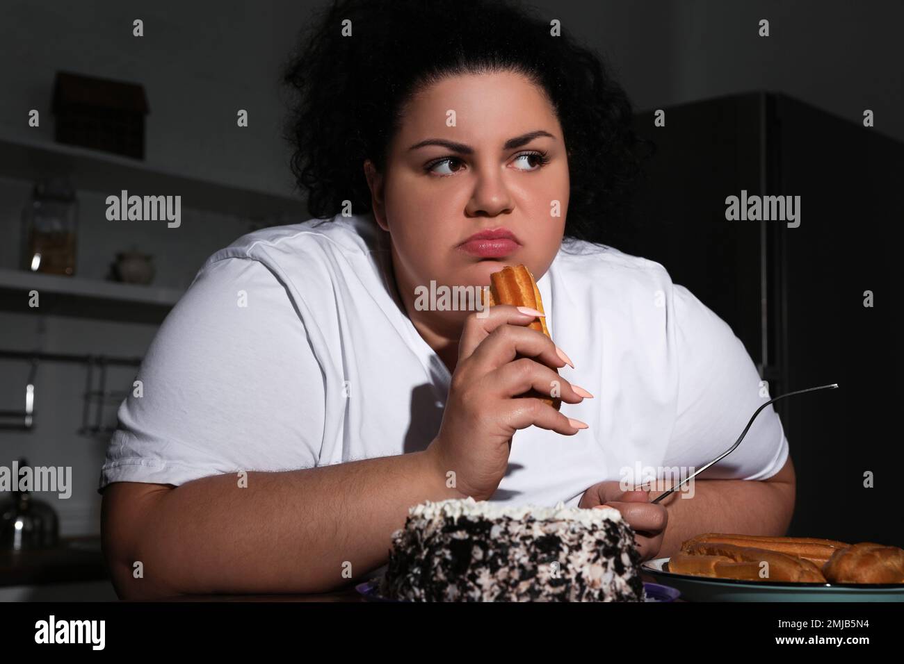 Depressed overweight woman eating sweets in kitchen at night Stock ...