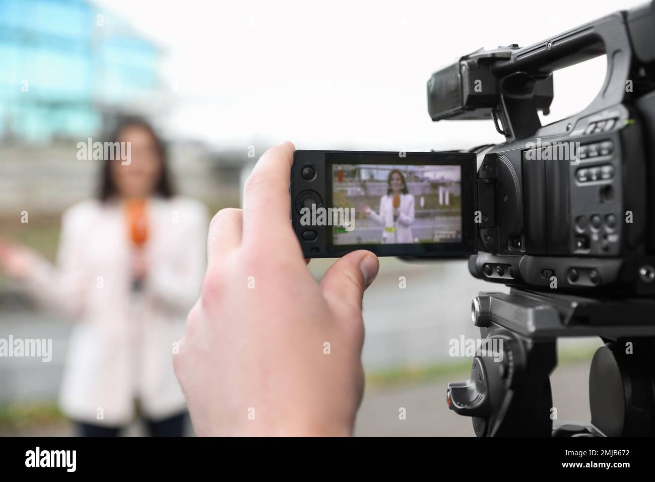 Young male journalist and video operator working on city street, focus ...