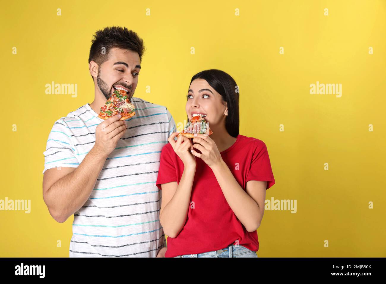 Emotional couple eating pizza on yellow background Stock Photo - Alamy