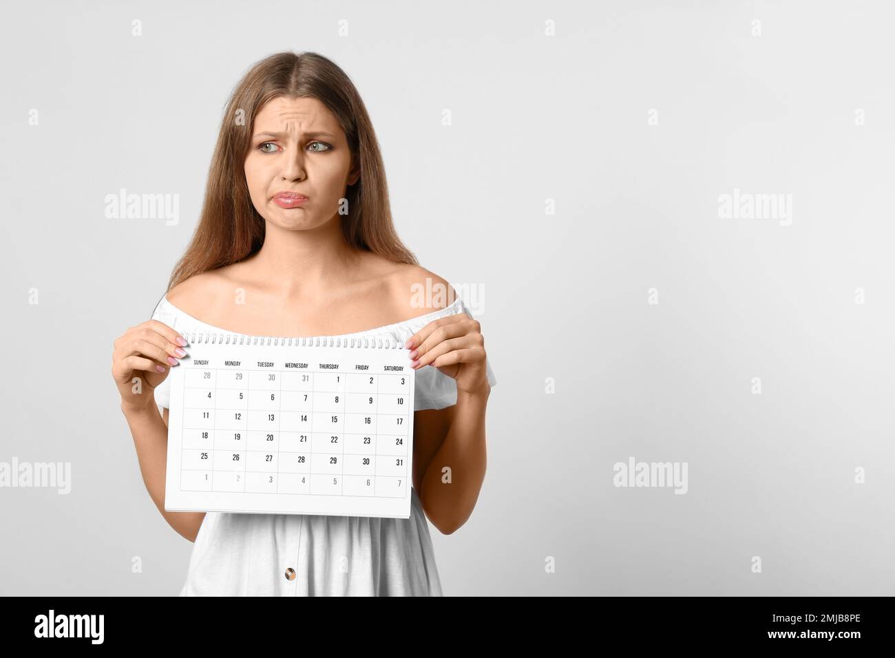 Emotional young woman holding calendar with marked menstrual cycle days ...